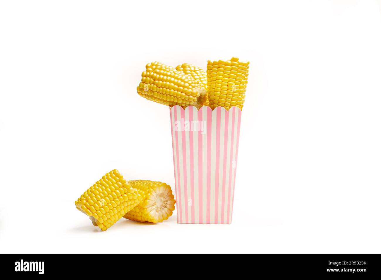 Pieces of corn in a pink and white striped bucket and on a white ...