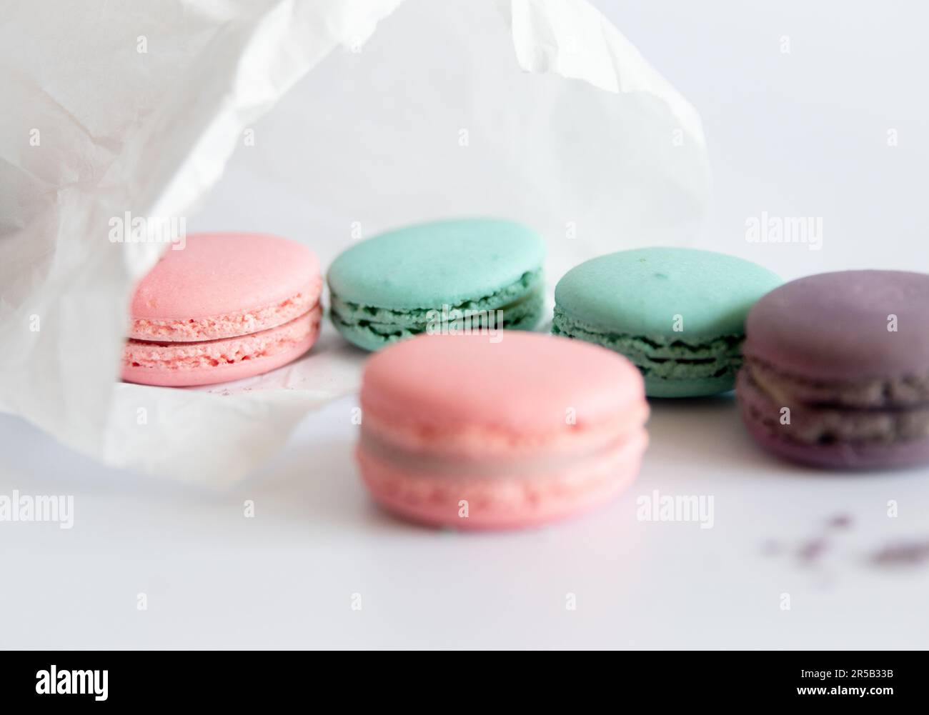 Multi-colored macarons falling out of white paper bag Stock Photo - Alamy