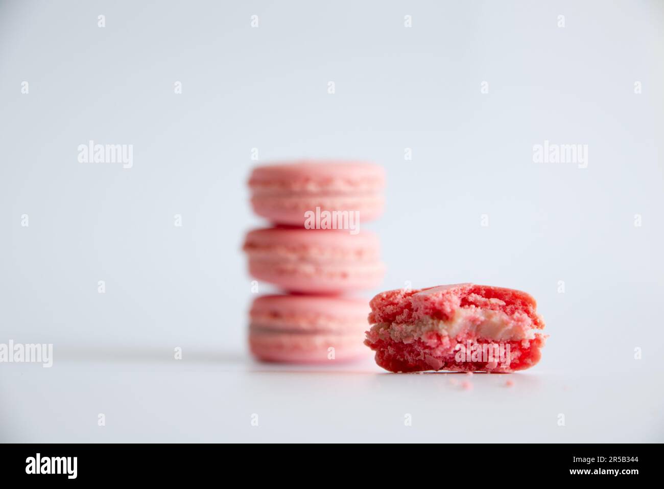 Stack of three pink macarons in the back and one bitten pink macaron in ...
