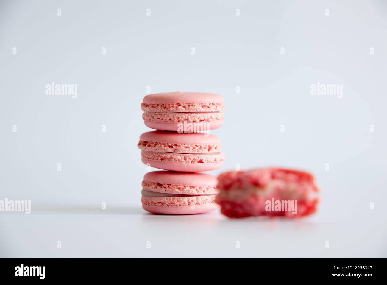 Stack of three pink macarons in the back and one bitten pink macaron in ...