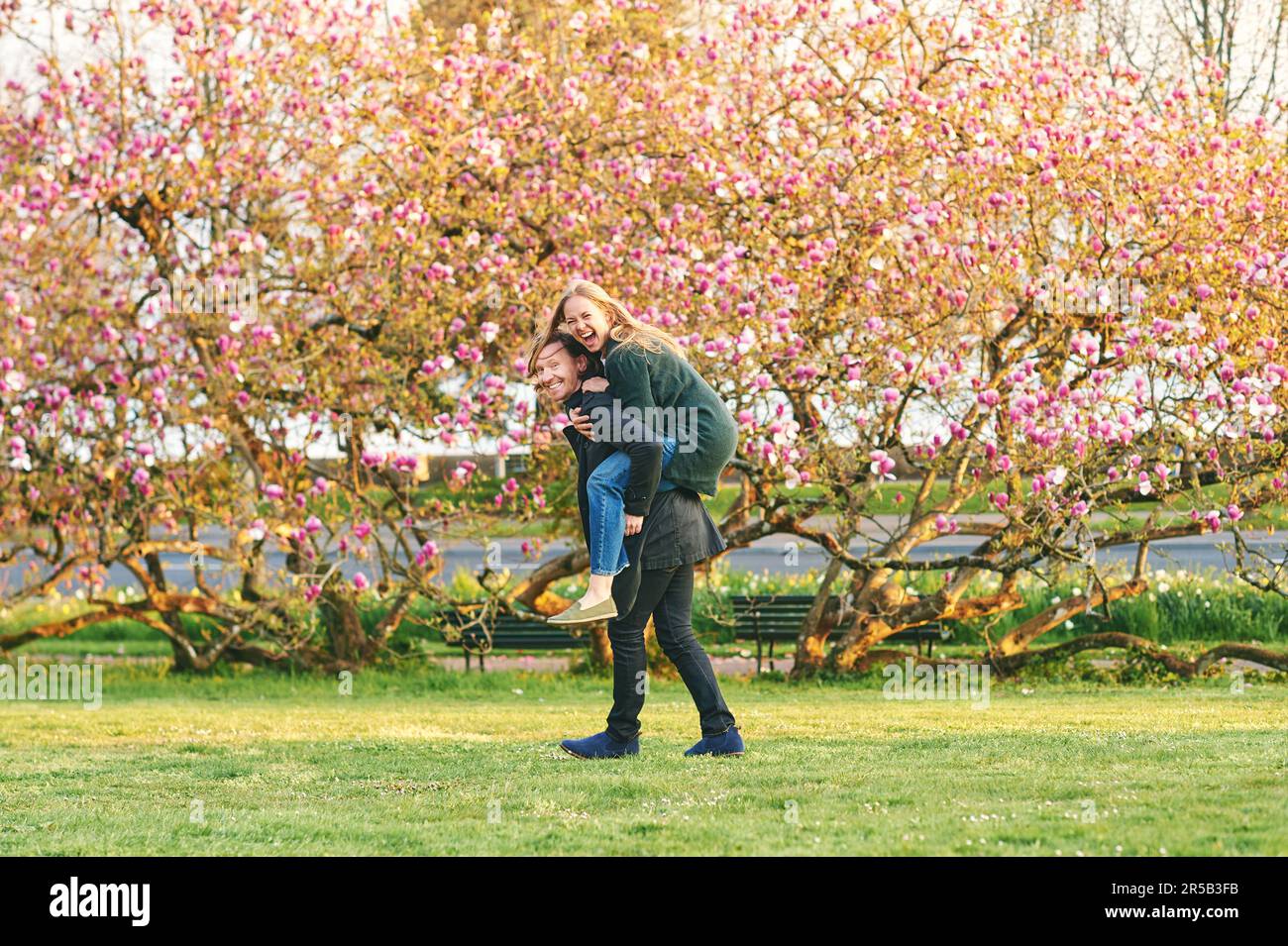 Outdoor portrait of happy romantic couple, woman sitting on back of her ...