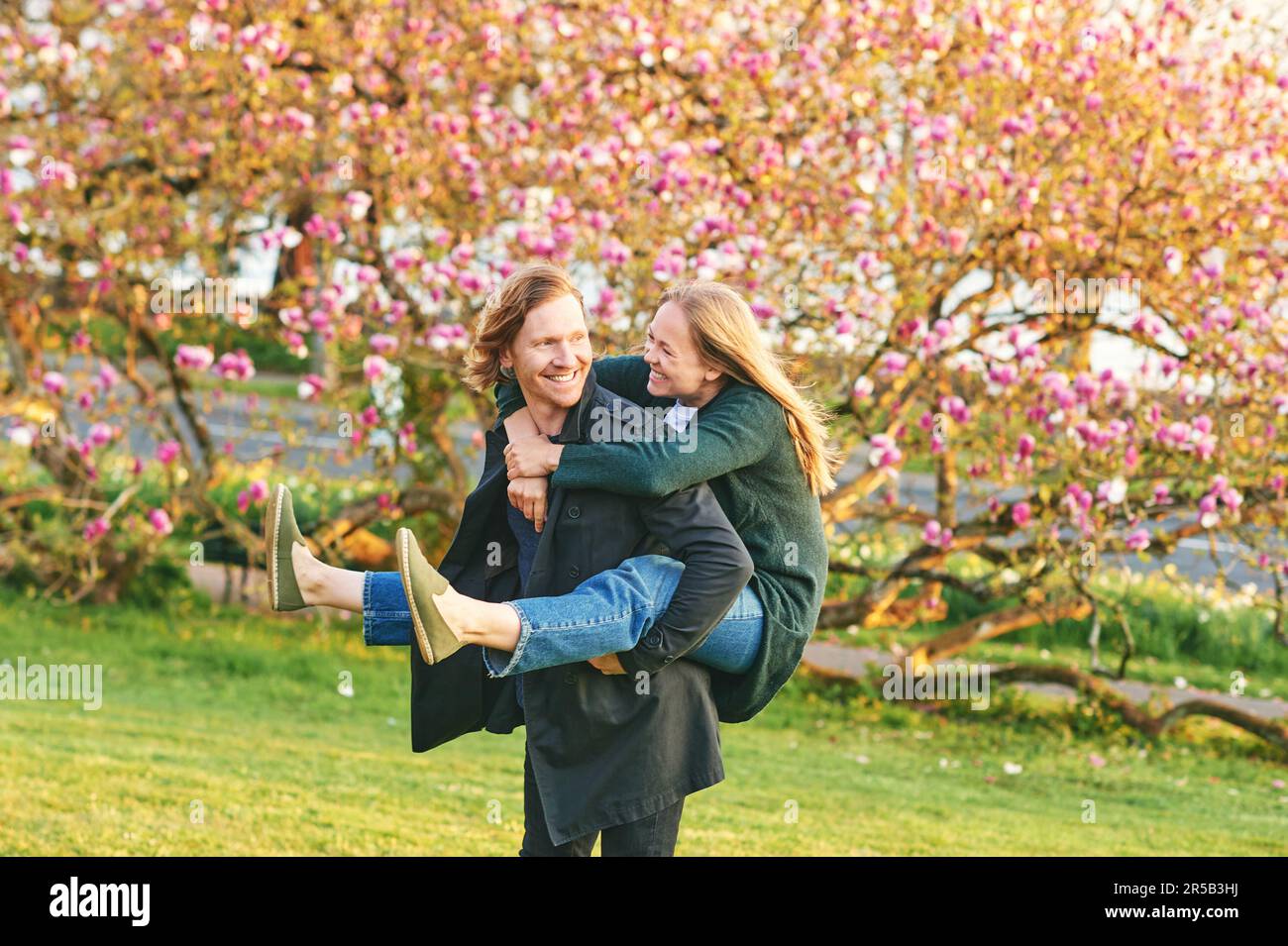 Outdoor portrait of happy romantic couple, woman sitting on back of her ...
