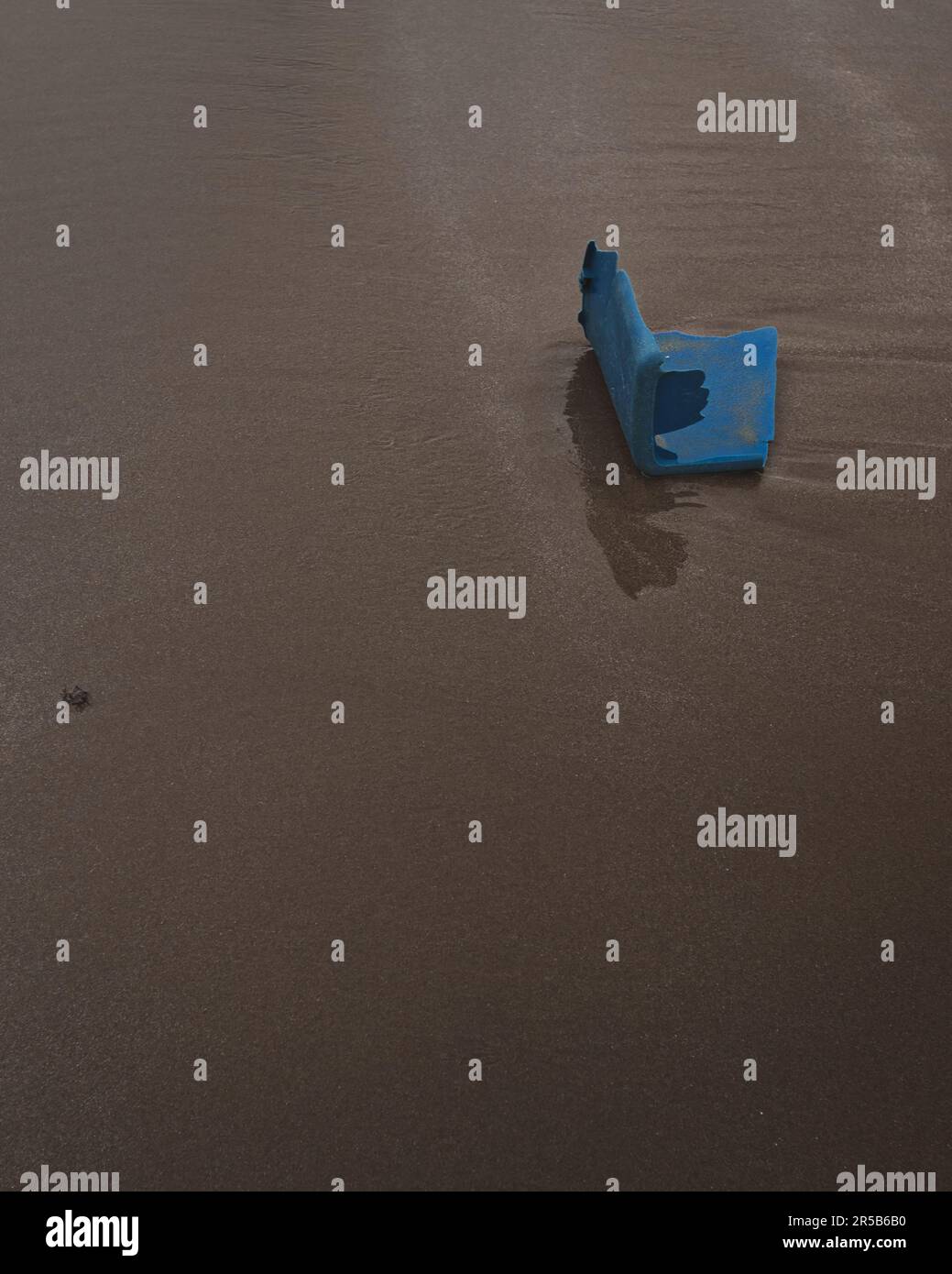 A bright blue plastic washed up on the sandy beach soaked in water ...