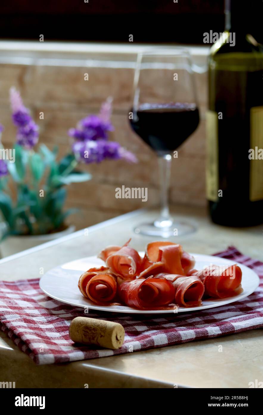Plate with sliced prosciutto and a glass of red wine on kitchen table ...