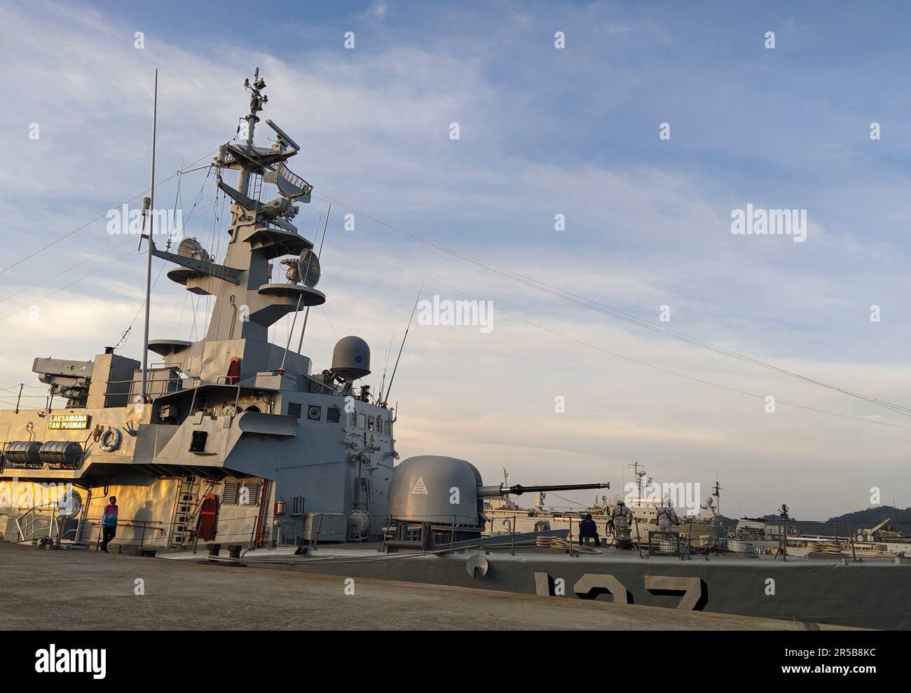 An aerial view of a navy ship docked at a port, with calm blue waters ...