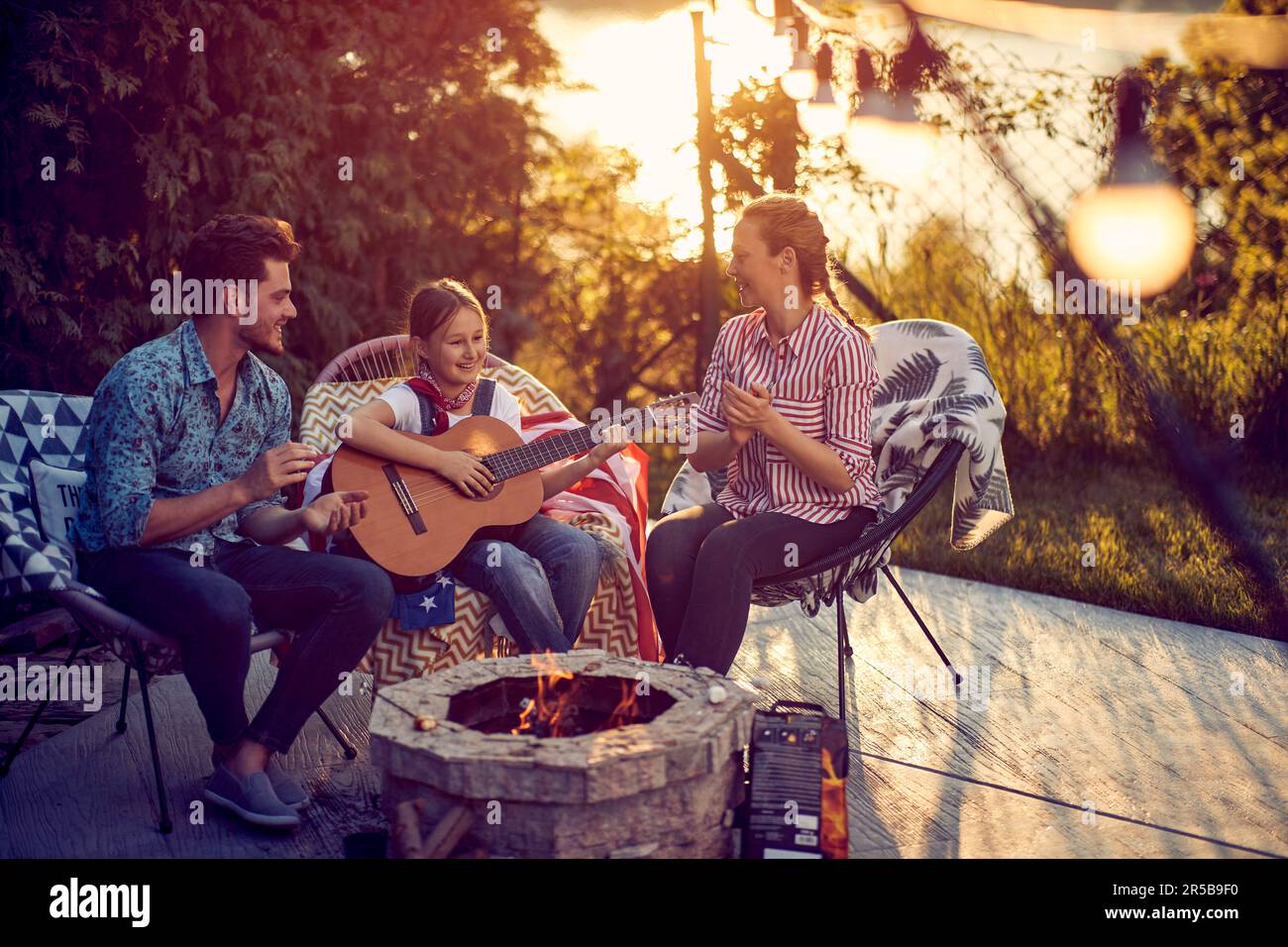 Little girl playing guitar by the fireplace, mom and dad clapping and ...