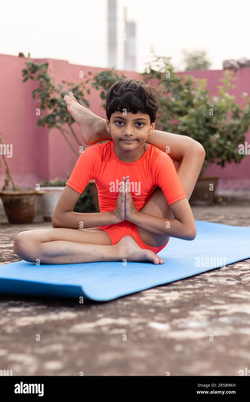 An Indian girl child practicing Ekpadasana yoga on yoga mat outdoors ...