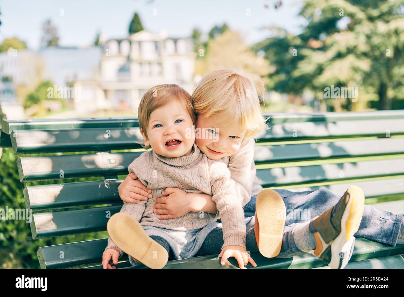 Outdoor portrait of two adorable siblings resting on the bench in sunny ...