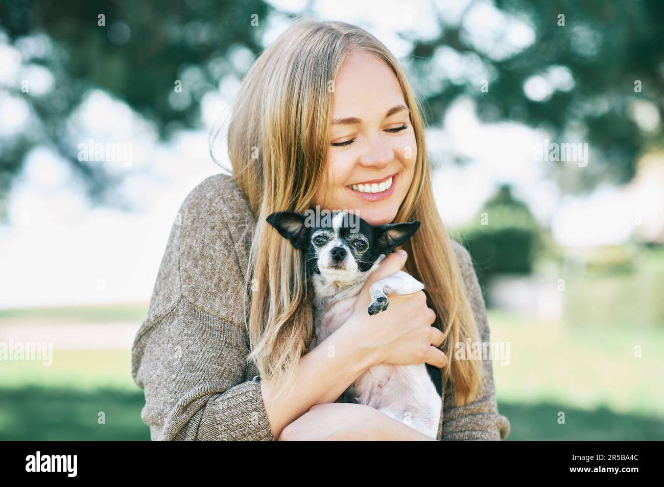 Outdoor portrait of happy young woman hugging small chihuahua black and ...
