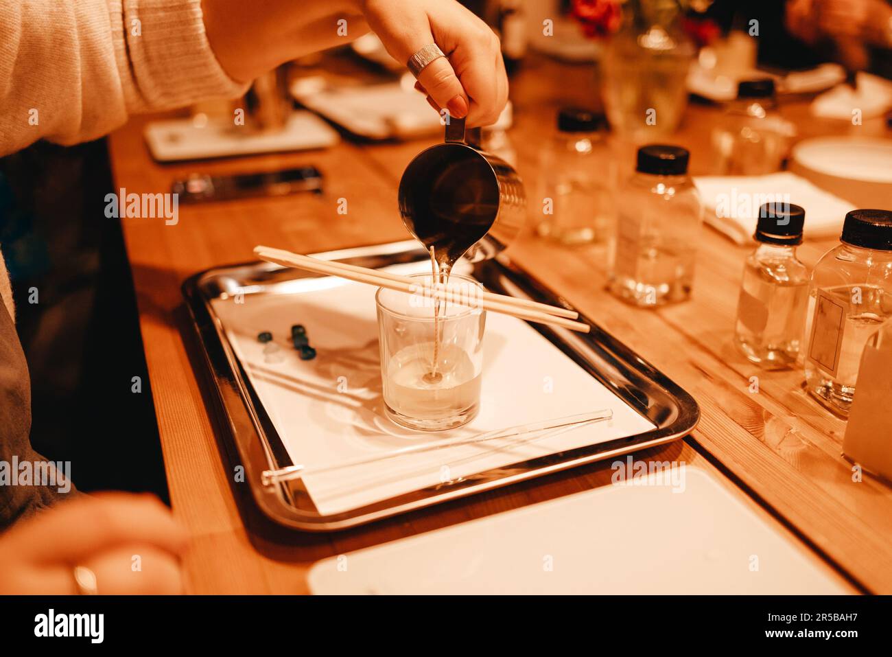 Pouring melted wax into glass. Set for crafting candle on metal tray ...