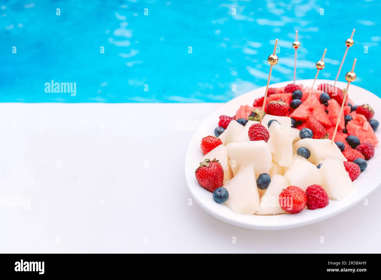 White oval plate with delicious fruits and berries against poolside ...