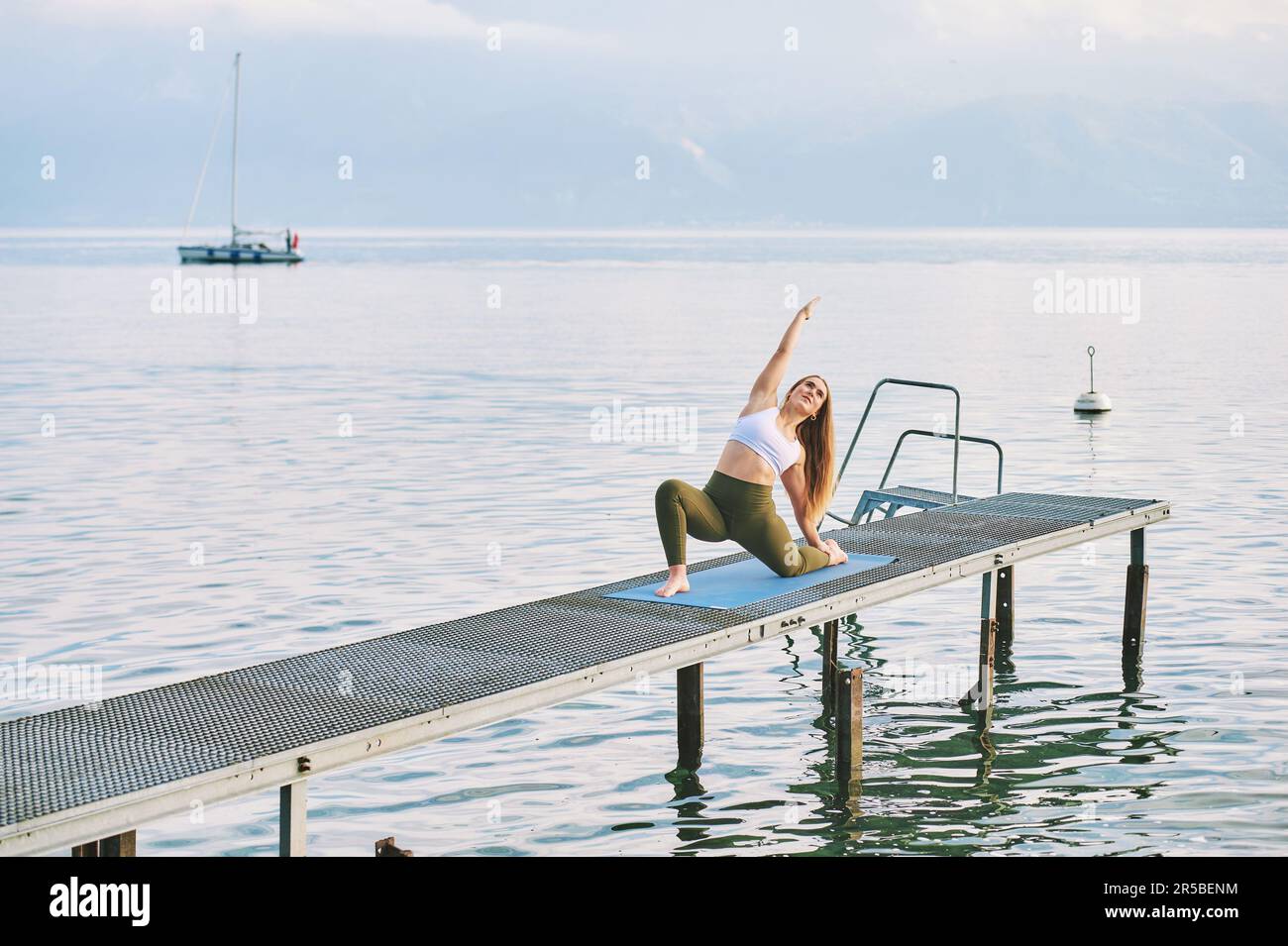 Outdoor portrait of young beautiful woman practicing yoga on dock by ...