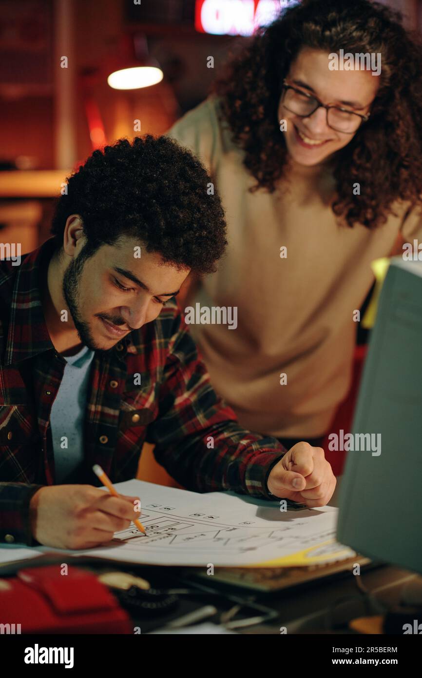 Young guys drawing business plan on paper together during their work in ...