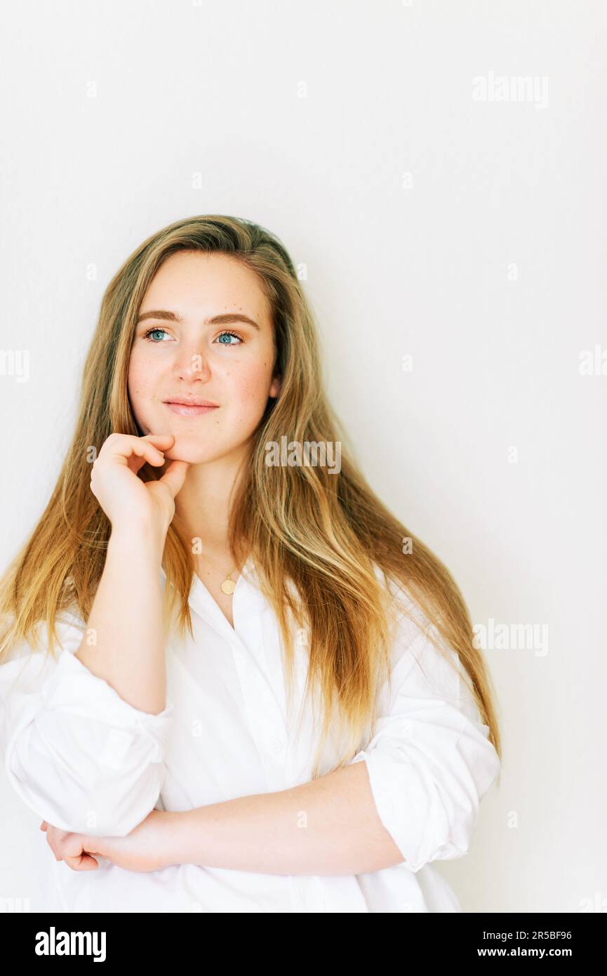 Indoor portrait of happy young female model, 20 year old girl wearing white shirt, healthy long ...