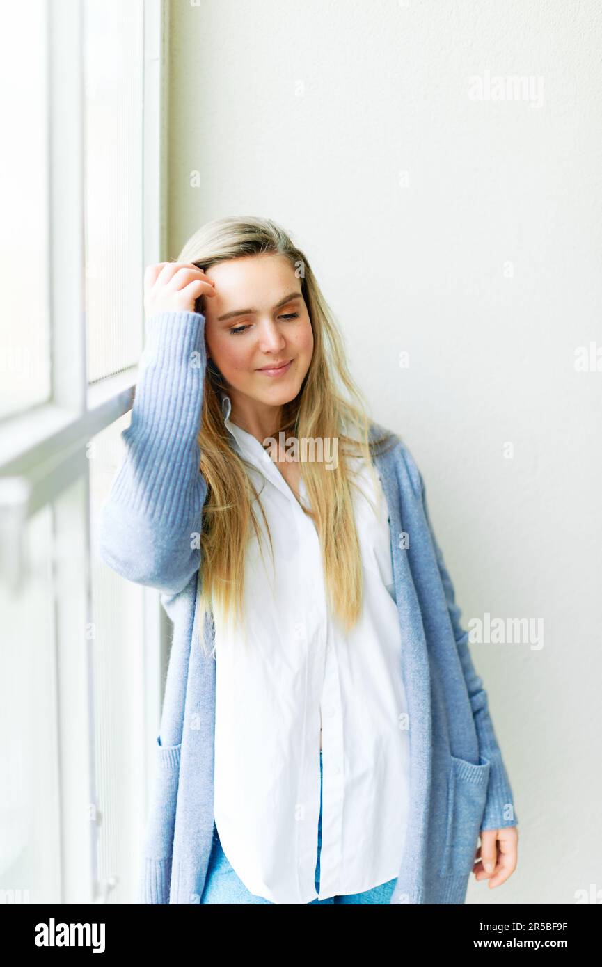 Portrait of young pretty 20 year old girl posing next to big window ...