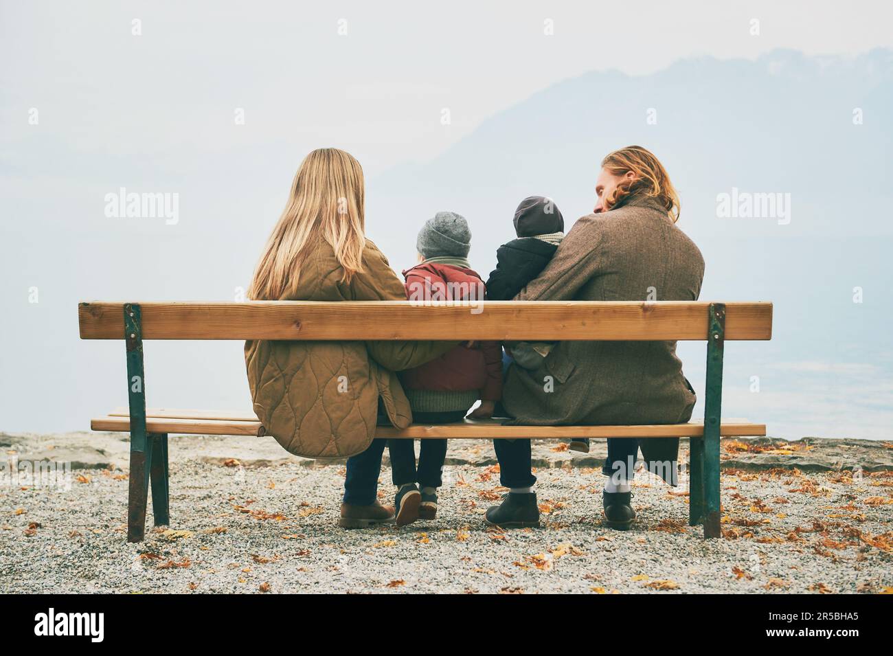 Family of 4 sitting on bench, enjoying nice autumn day by the lake ...