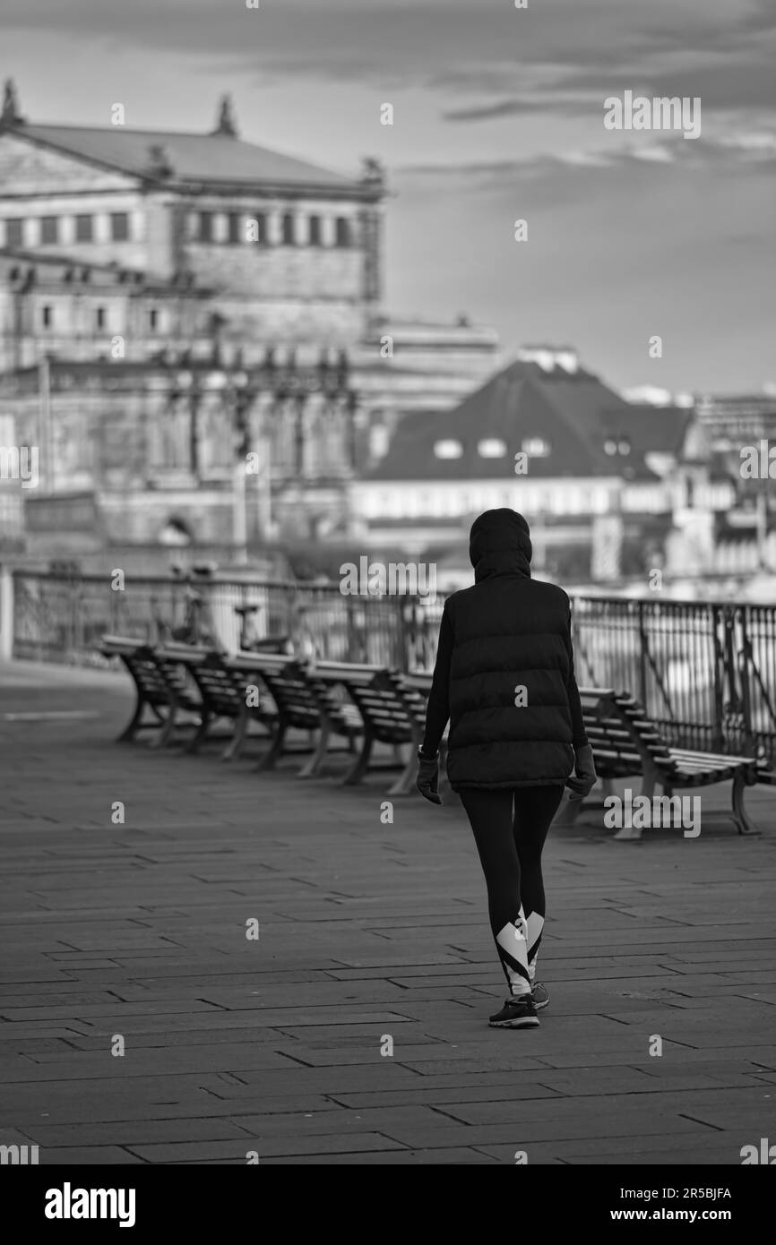 A grayscale of a person walking on the urban street scene with benches ...