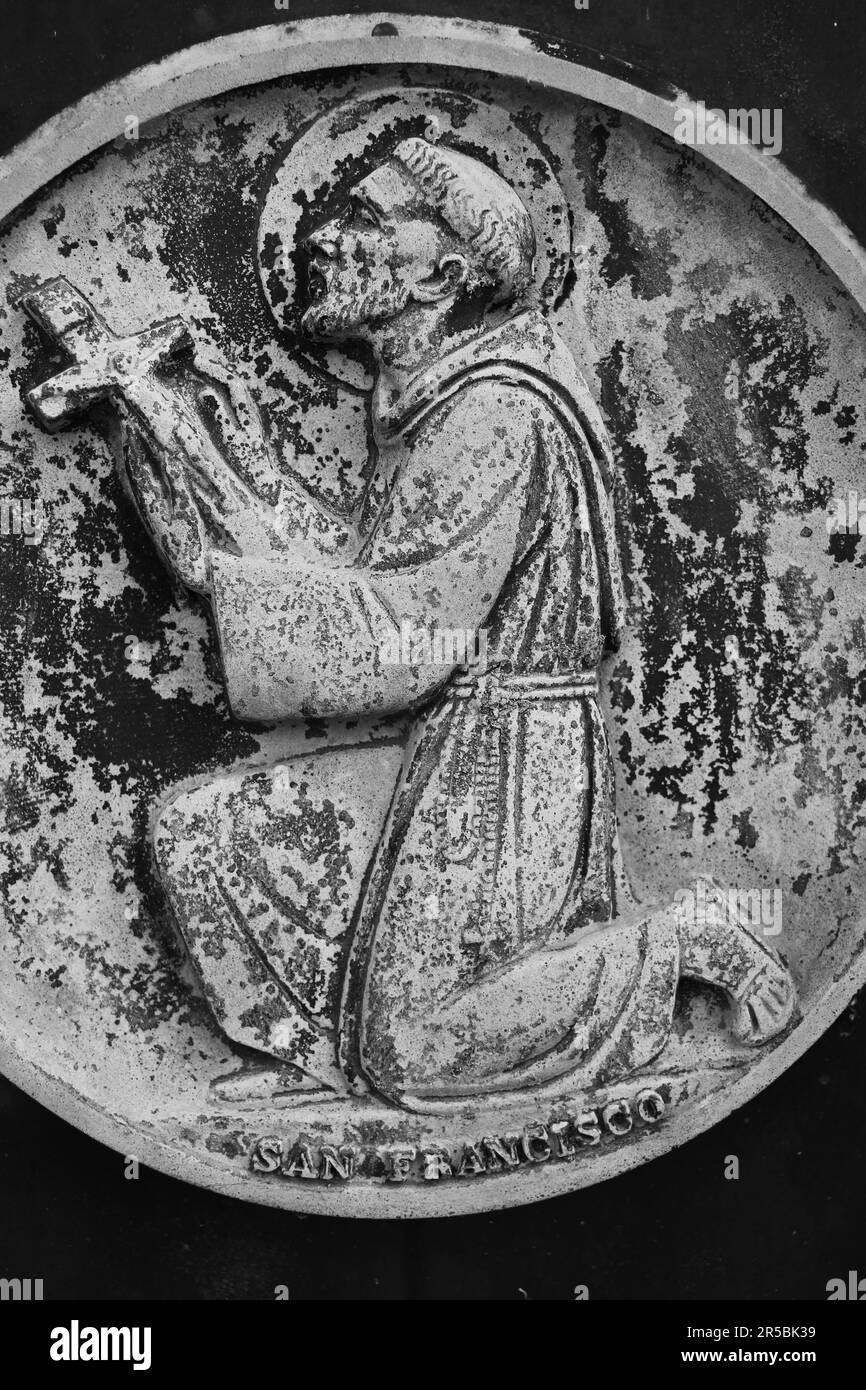 A carving of San Francisco kneeling in prayer and holding a cross in a ...