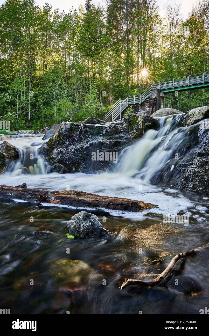A brook cascading down rocks with a wooden bridge visible in the ...