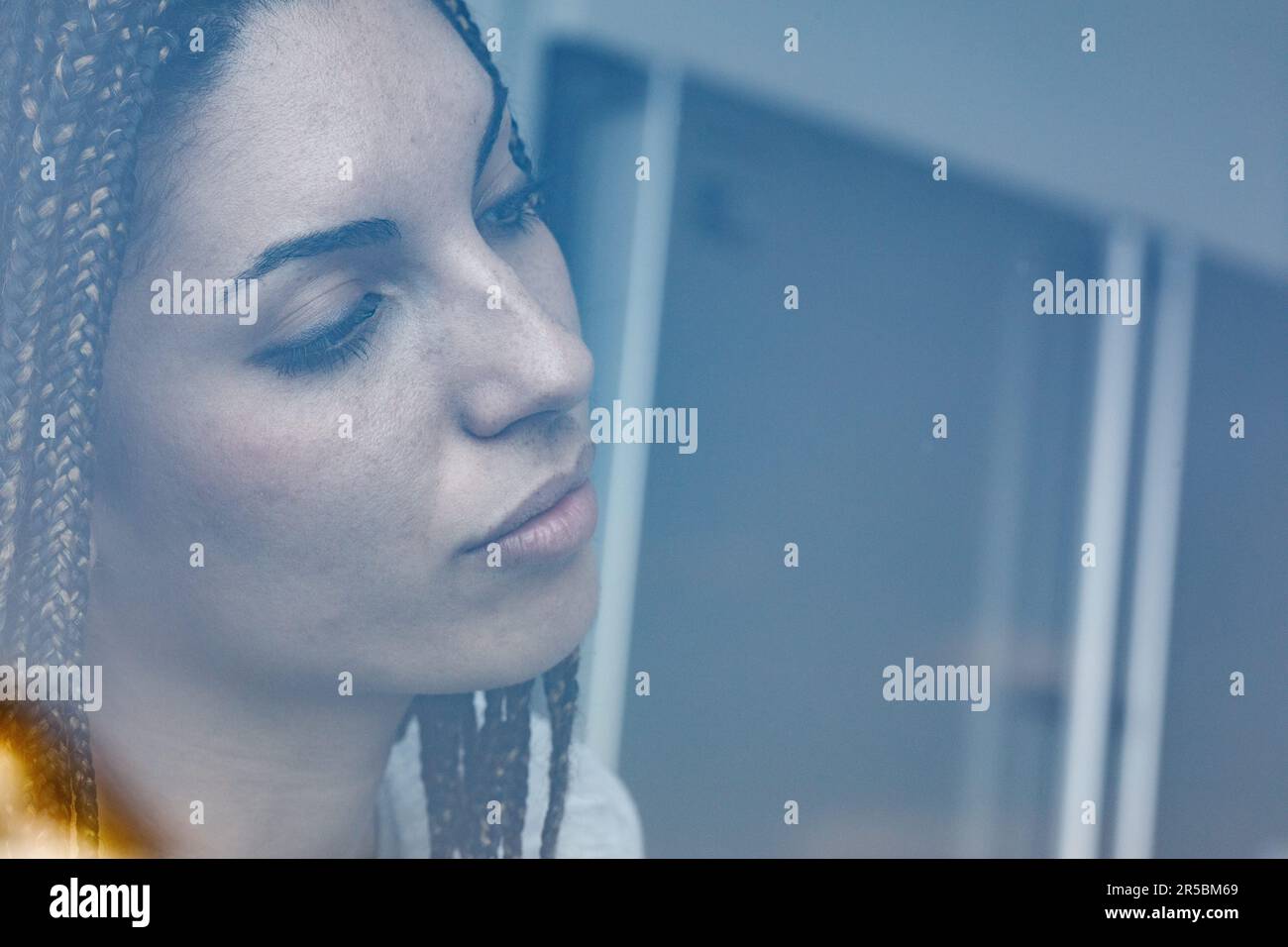 Young woman with box braids looks longingly outside from behind a ...