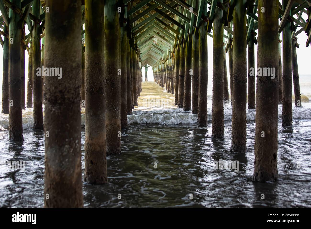 The sun shining through a pier at Myrtle Beach, SC as the surf rolls in ...