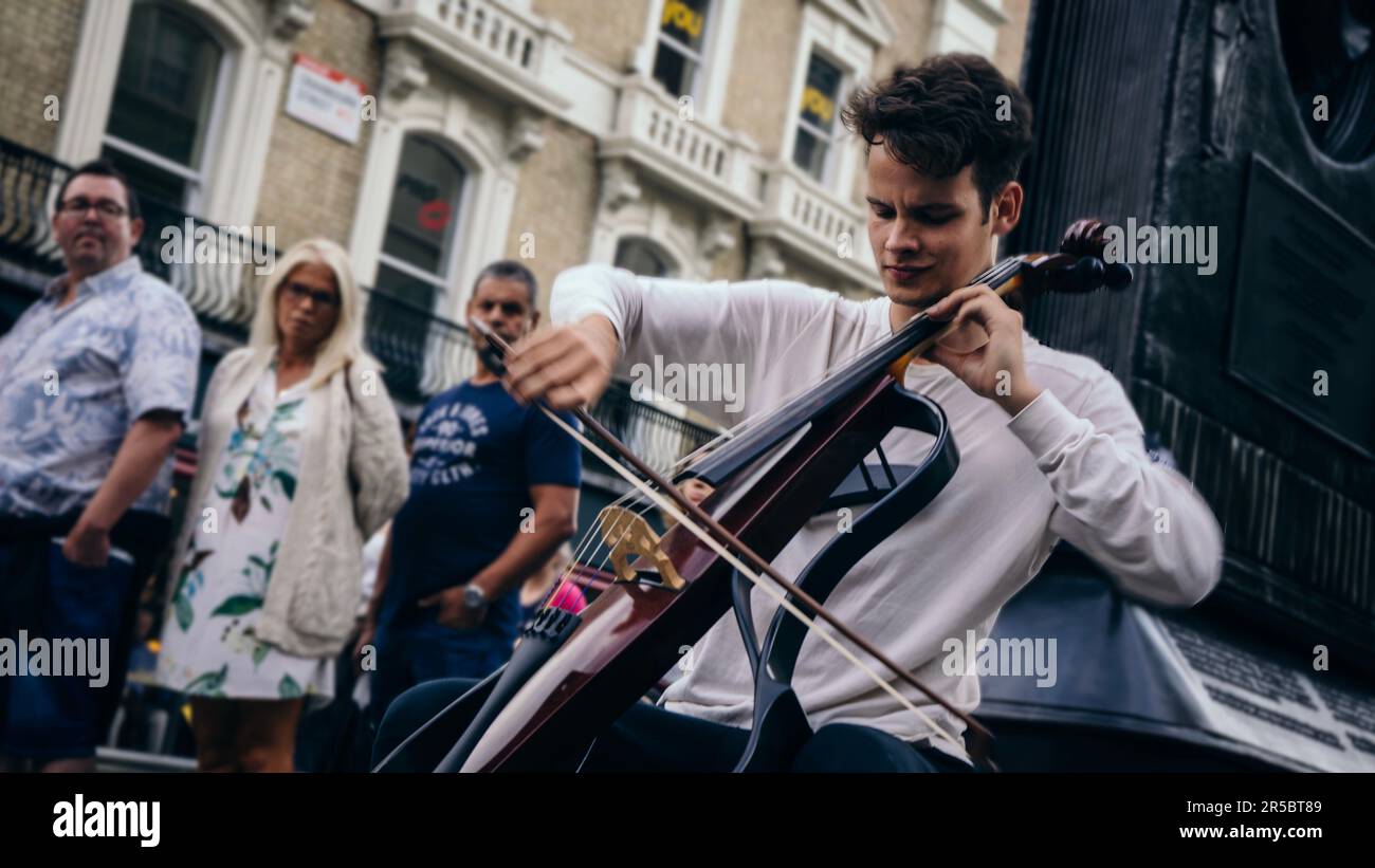 A handsome young man wearing playing a musical instrument in the street ...