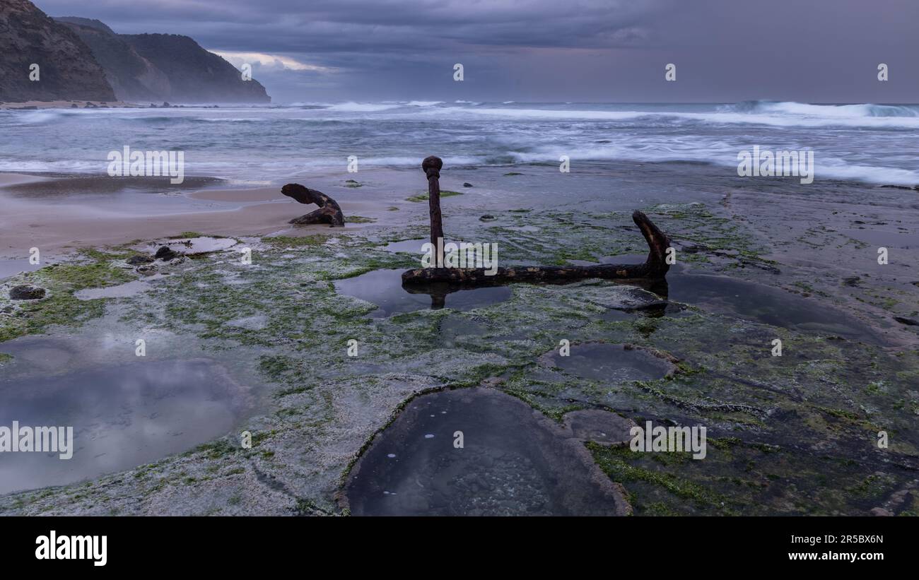Two rusty anchors laying on the ground in a coastal setting, near the ...