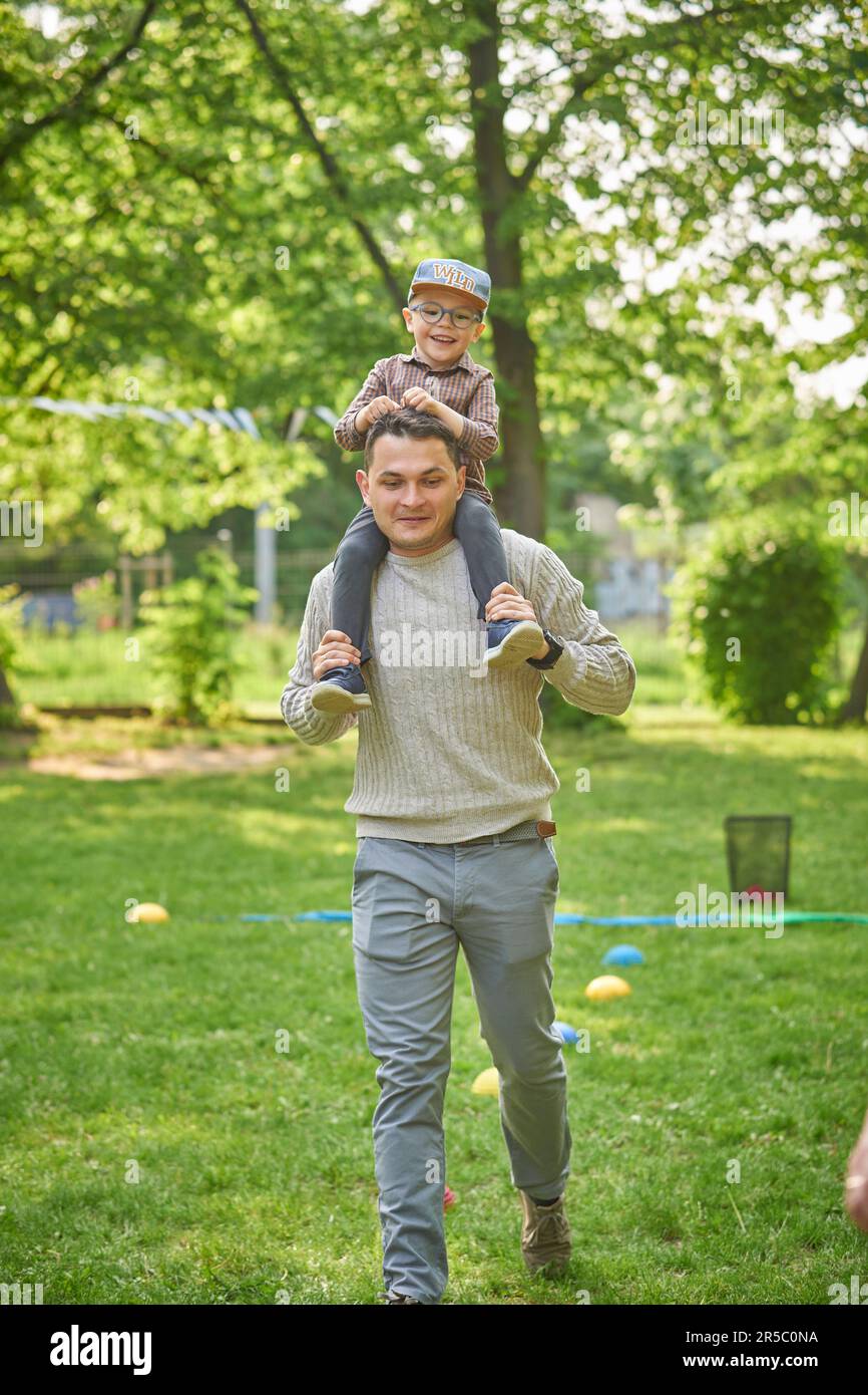 A happy father carrying his son on a piggyback ride in a public park ...