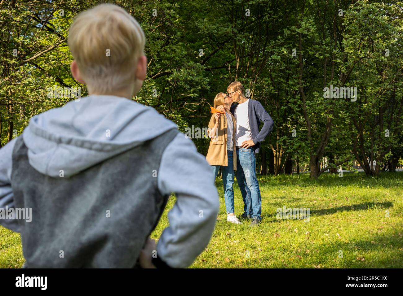 Back View OF Emotional Caucasian Boy Looking At Kissing Parents in Park ...