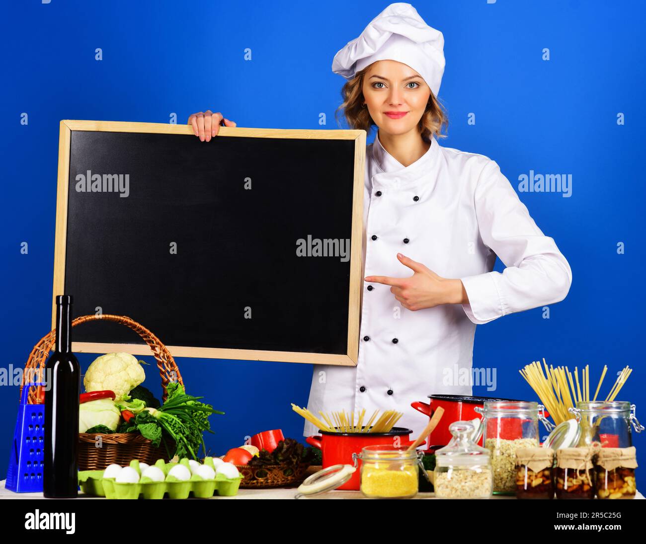 Woman chef pointing finger to blank blackboard. Food preparation ...