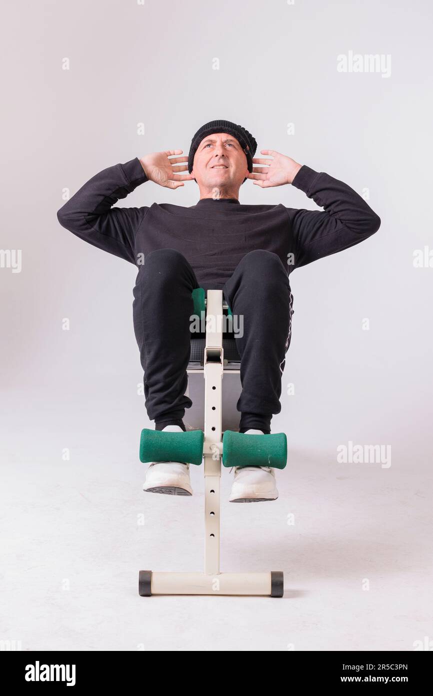 A Caucasian male doing sit up exercise with machine against a white ...