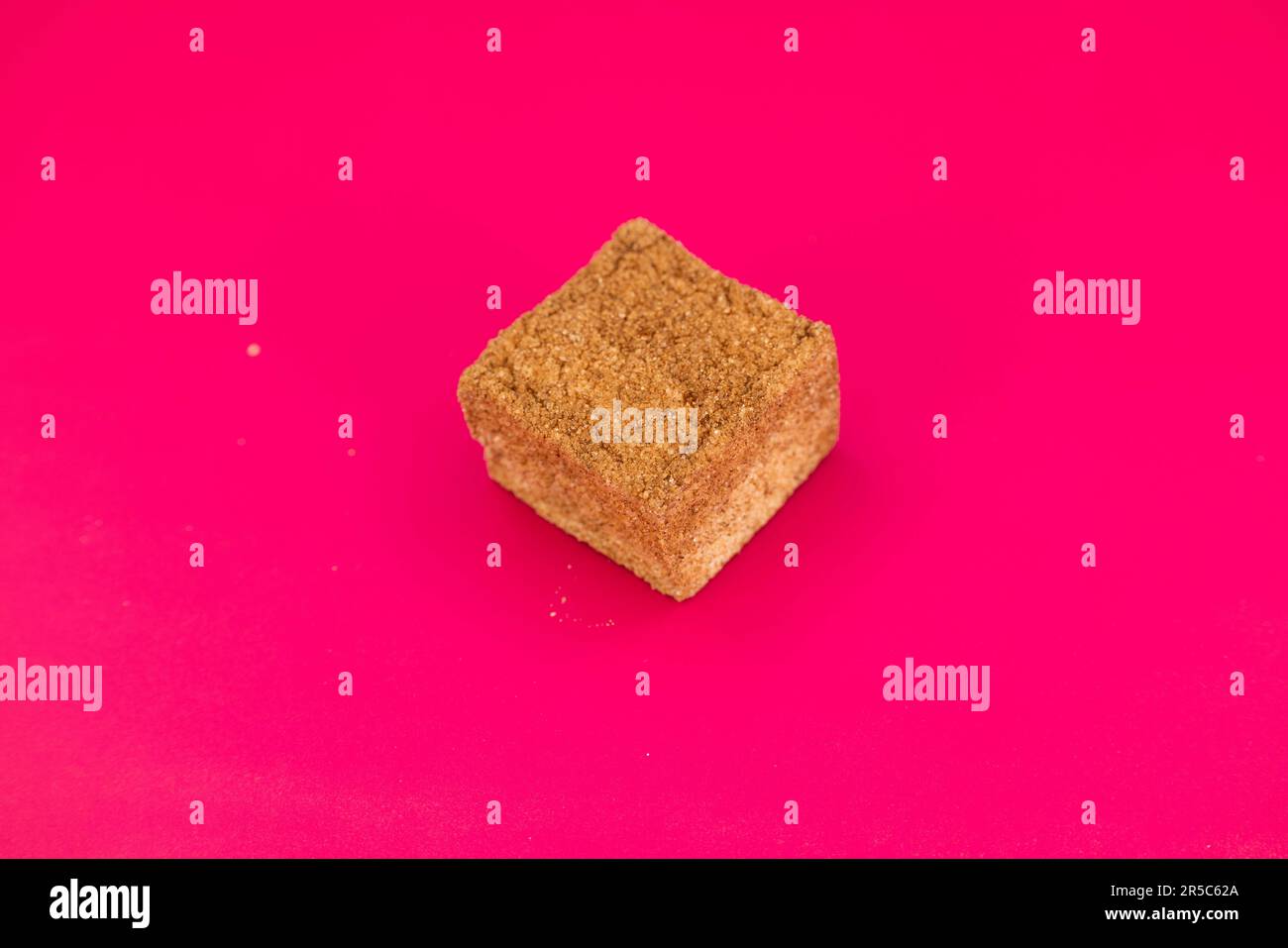 A freshly-baked square pastry on a solid pink surface, topped with a ...