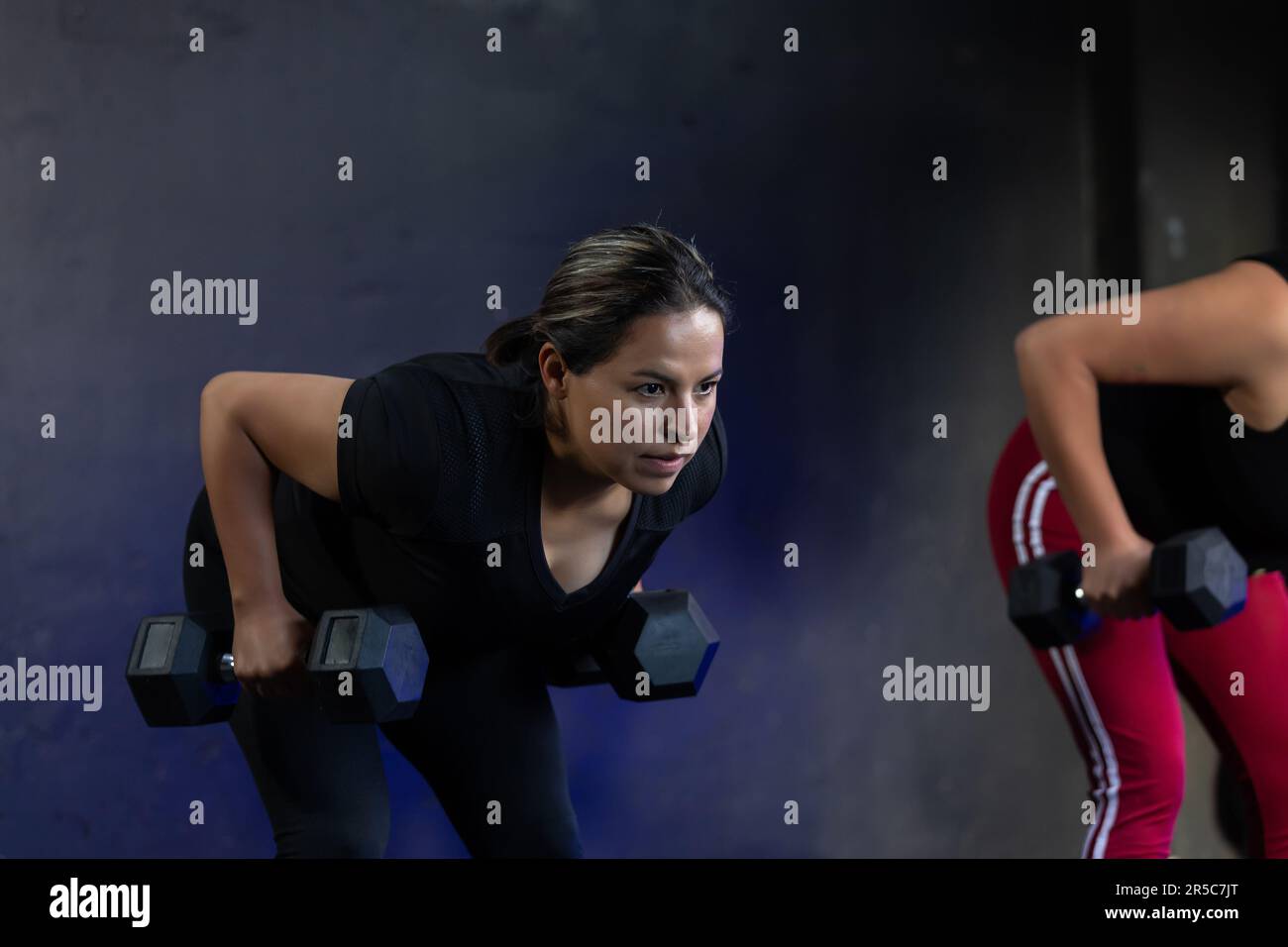 Two young female friends working out in a gym, lifting weights with ...