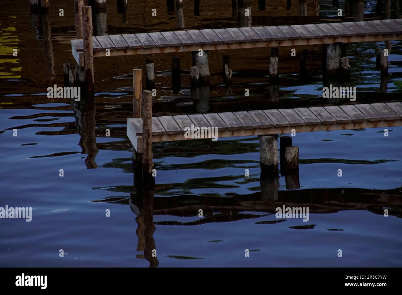 An idyllic dock featuring a small pier with wooden poles protruding out ...