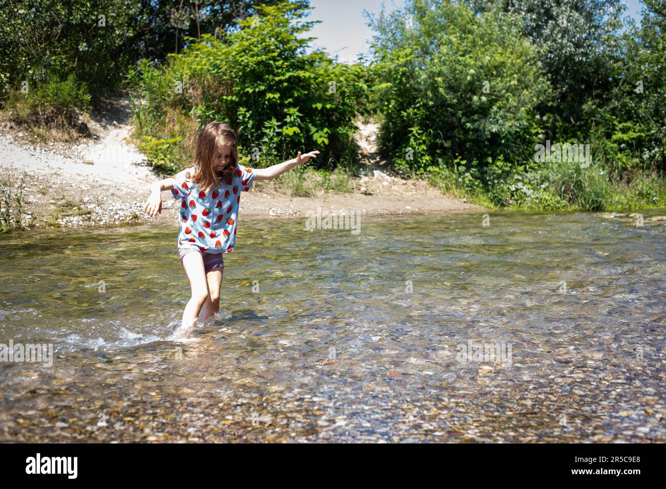 Caucasian child girl wading a clear stream on a bright sunny day. Parco ...