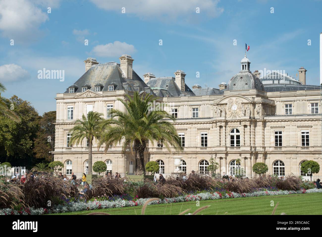 A historic building with trees and people in the gardens in Paris ...