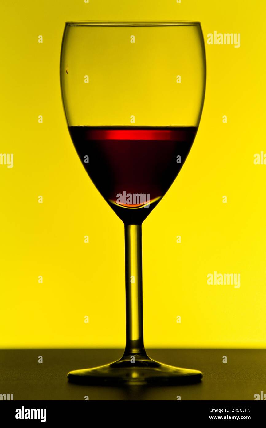 Red wine glass on table with yellow background and strong contrast ...