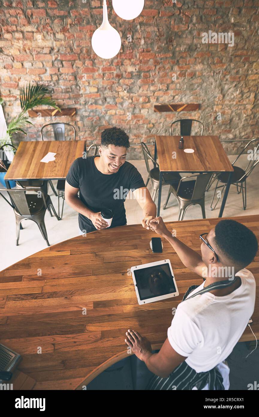 The friendliest barista on the block. a young man serving a customer coffee and giving him a ...