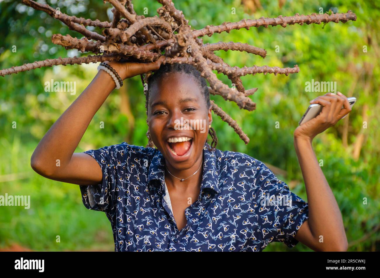 young African girl carrying wood and a and using her phone on a farm ...