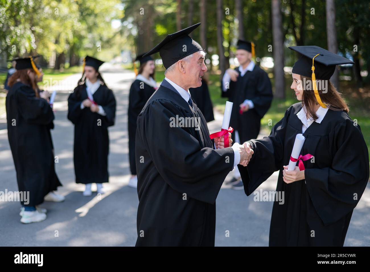 A group of graduates in robes outdoors. An elderly man and a young ...