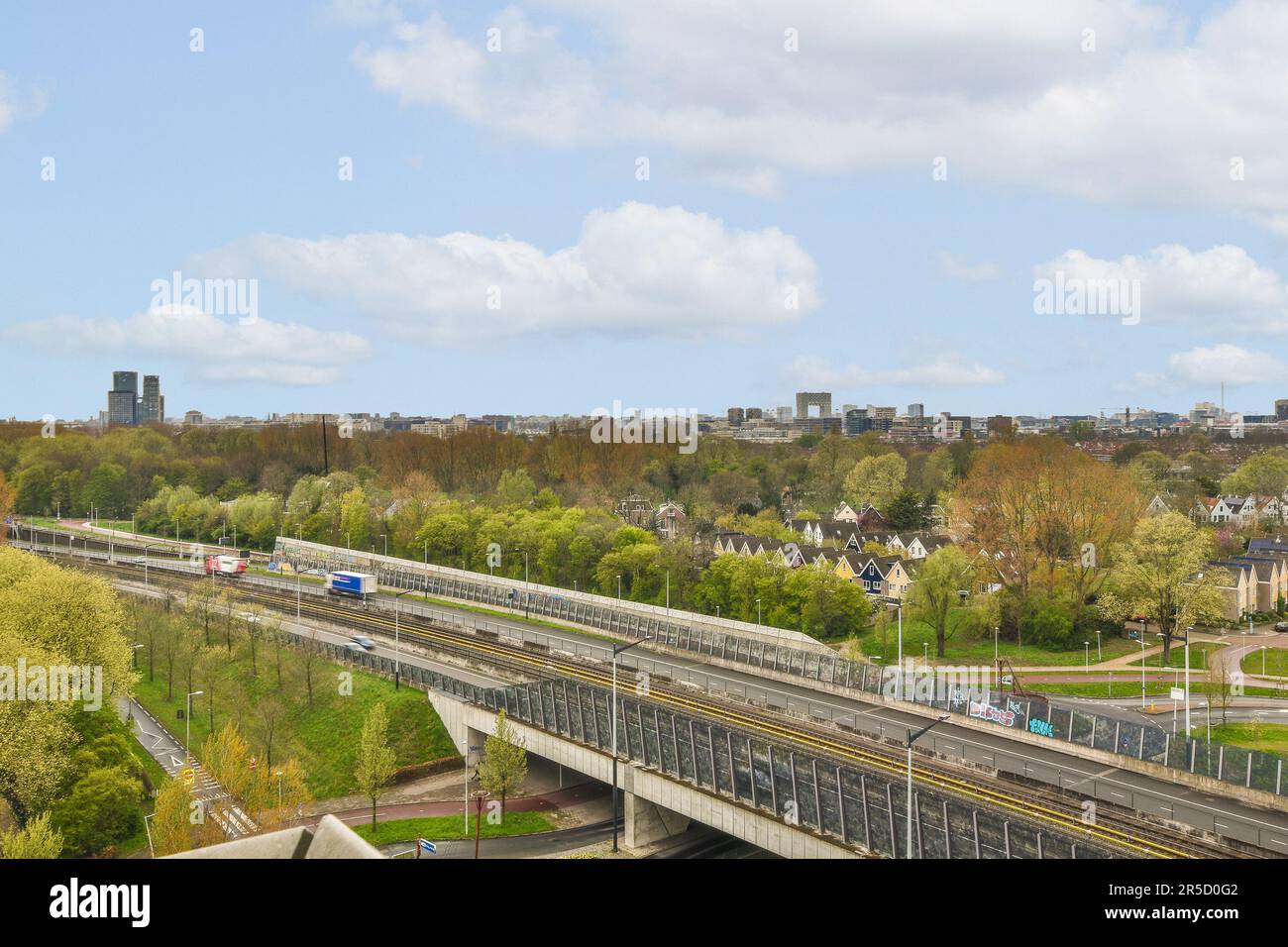 a train going over a bridge with buildings in the background and trees ...