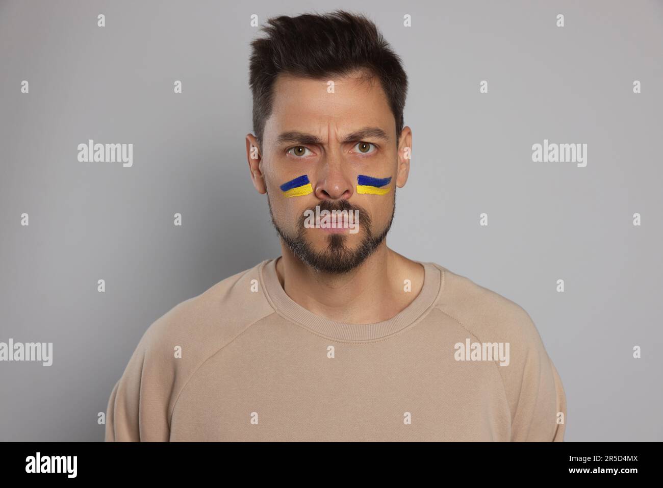 Angry man with drawings of Ukrainian flag on face against light grey ...