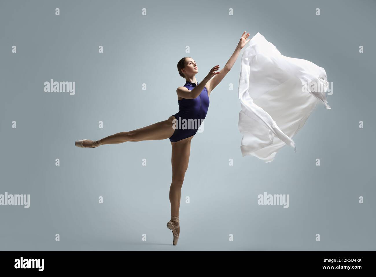 Graceful young ballerina practicing dance moves with veil on grey ...