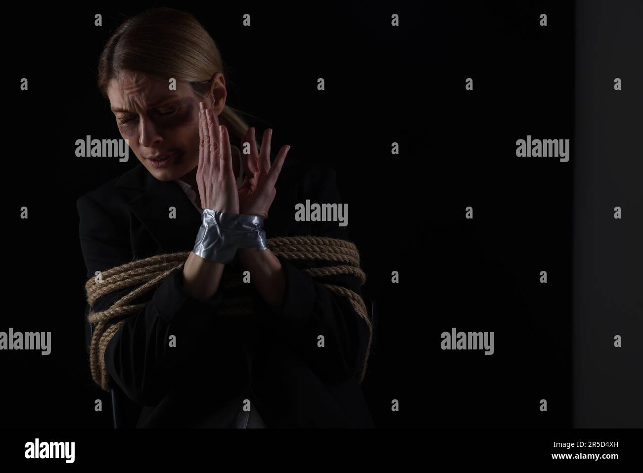Scared woman tied up and taken hostage on dark background. Space for ...
