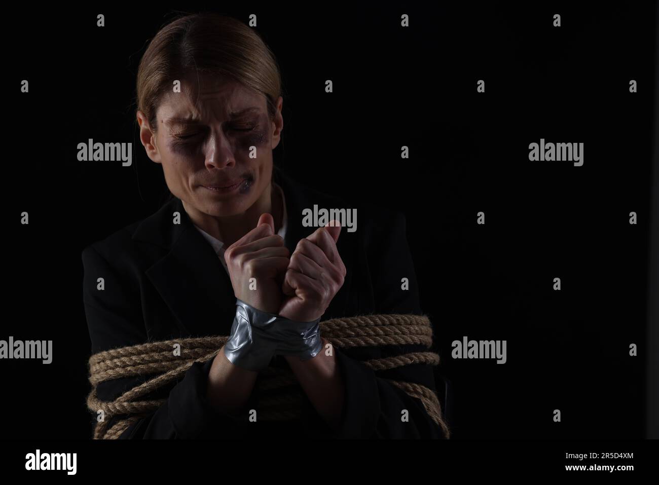 Scared woman tied up and taken hostage on dark background. Space for ...