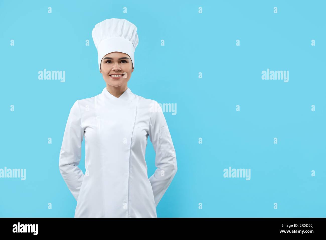 Happy female chef wearing uniform and cap on light blue background ...
