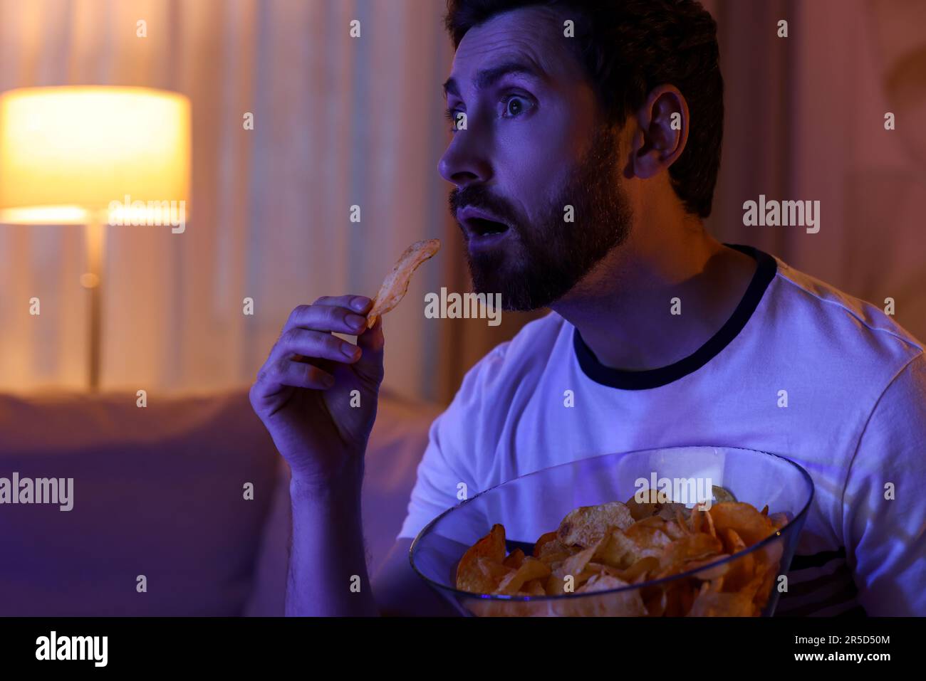 Man eating chips while watching TV on sofa at night. Bad habit Stock ...