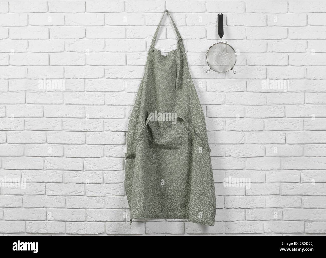 Clean kitchen apron with pattern and sieve on white brick wall Stock ...
