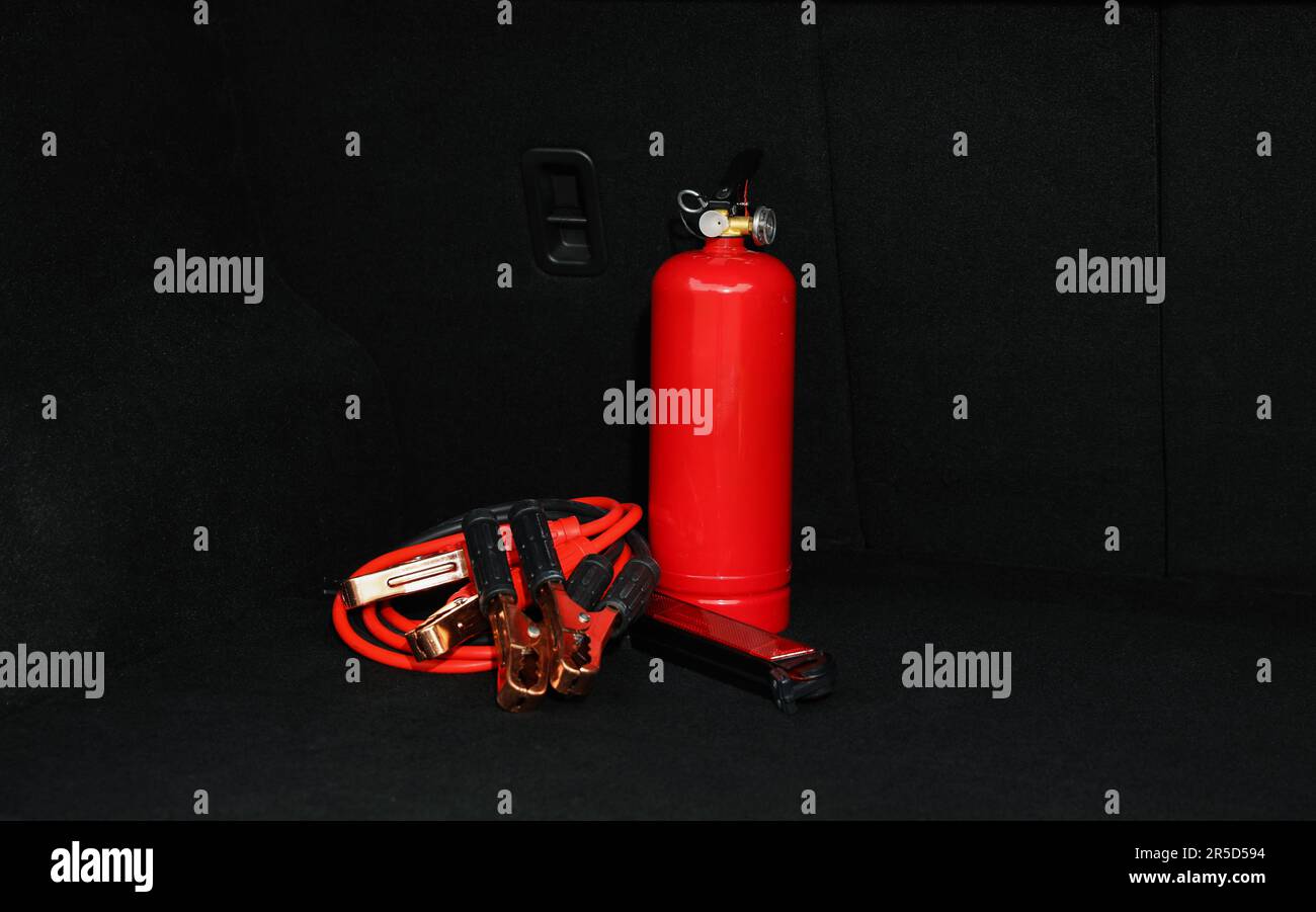 Red fire extinguisher and battery jumper cables in trunk. Car safety ...