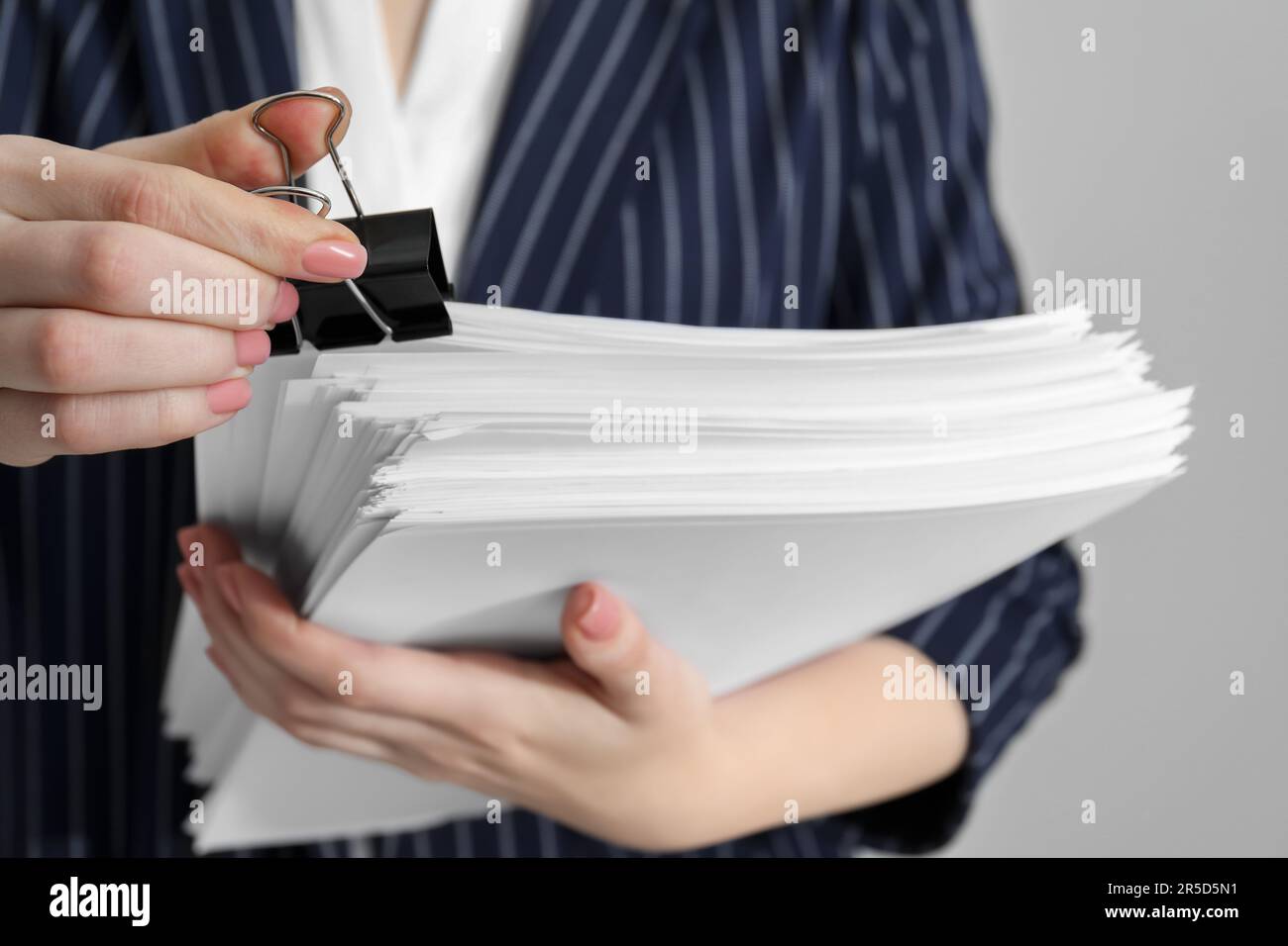 Woman attaching documents with metal binder clip on grey background ...